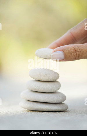 Hand placing a stone on a rock surface with small pebbles in an outdoor ...