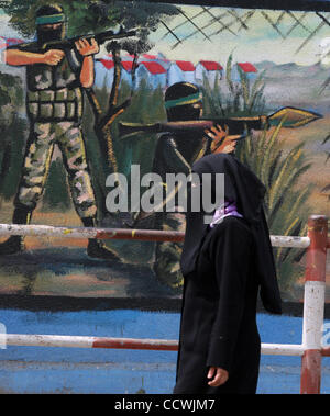 A Palestinian woman walks in front of a wall painting depicting ...