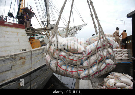Workers load sacks of rice onto a traditional cargo ship for domestic ...