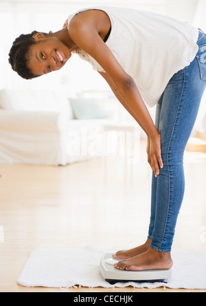 Young black woman weighing herself on medical scale on green screen ...