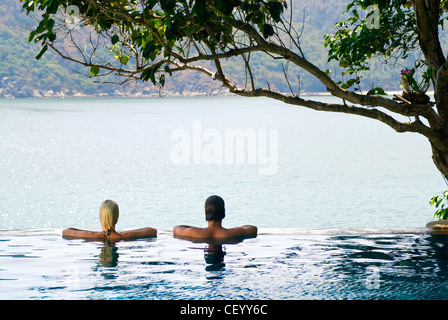 A young couple enjoys a romantic swim together at a tropical resort ...