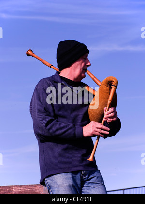 Busker man playing bagpipes with a single drone on Whitby West Cliff ...