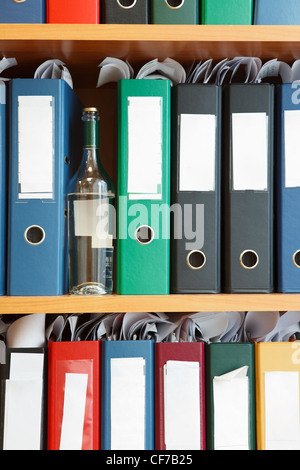 Glass bottle with alcohol hidden between file binders on shelves Stock ...