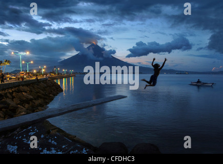 Boy jumping into the sea before a glowing Mayon Volcano Stock Photo - Alamy