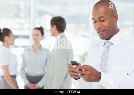 Salesman writing text message with team behind him Stock Photo - Alamy