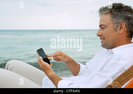 partial view of man using smartphone with blank screen on sandy beach ...