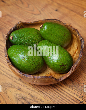 Avocados in wooden carved bowl, one of them cut in half, seed visible ...
