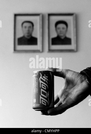 Can of North Korean coca cola in front of the portraits of Kim il Jong ...