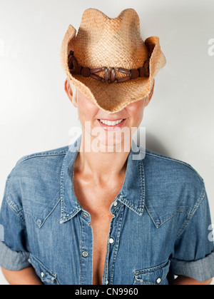 Smiling woman wearing a straw hat and sunglasses, peering through a ...