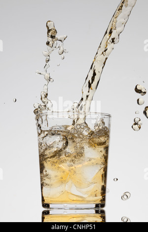 Stream of soda being pouring into a glass with soda and ice cube on black background, closeup ...