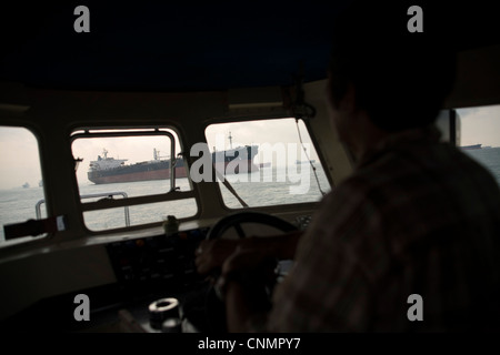 A boat driver navigates past one of the several hundred ships at anchor ...