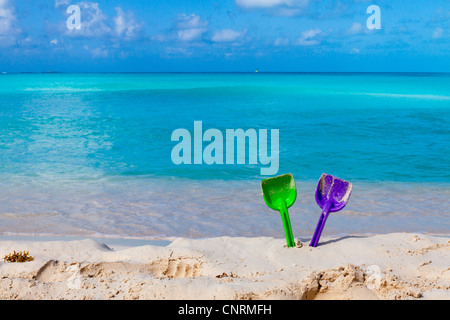 Pair of colored spades on a white sand beach in front of the sea. The ...