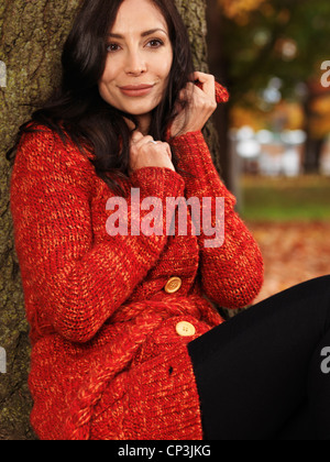 trendy brunette woman in knitted sweater standing with hands in pockets ...