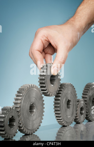 Man adding a cog gear wheel into a row of old cogs Stock Photo - Alamy