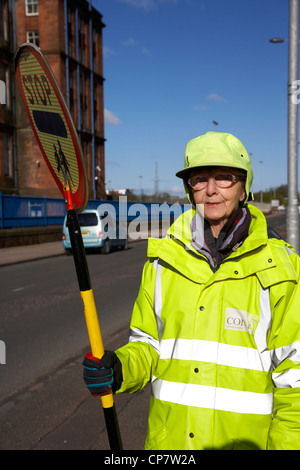 A British lollipop lady or crossing guard stopping traffic outside a ...