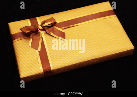 A gift wrapped in black and gold tree-pattern paper with a red bow ...