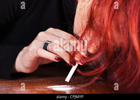 A young woman snorting a line of cocaine off a mirror through a rolled ...