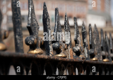 Rusty and ornate wrought iron fence with out-of-focus buildings in the ...