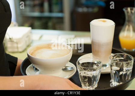 Server with cups of coffee on a tray in a cafe with young and elderly ...