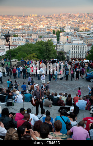 Busker performing to a crowd on young people sitting on the steps of ...