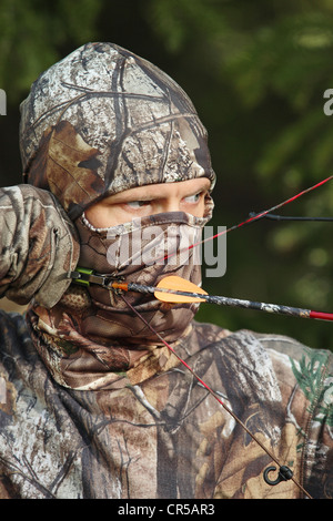 close-up bow hunter dressed in camouflage pulling bow back in woods ...