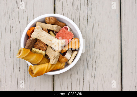 A bowl of dog food and treats in the form of bones on a wooden floor ...