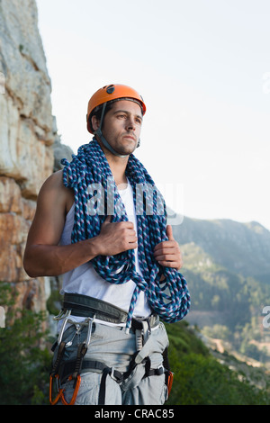 A rock climber coiling a climbing rope around his body preparing to ...
