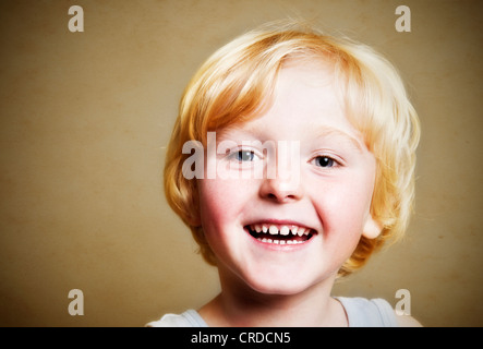 A portrait of a smiling five year old boy with brown hair, wearing a ...