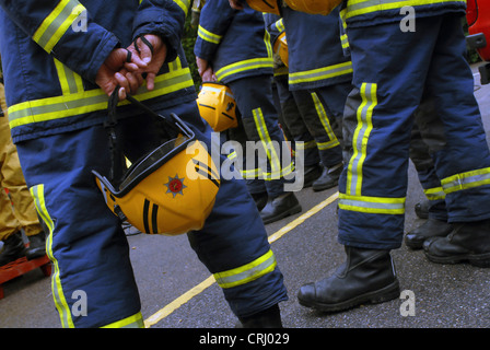 Firefighters in uniform stand by a fire truck with a ladder, looking ...