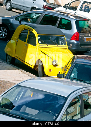 A bright Yellow 2CV car parked on a street next to a yellow Laburnum in ...
