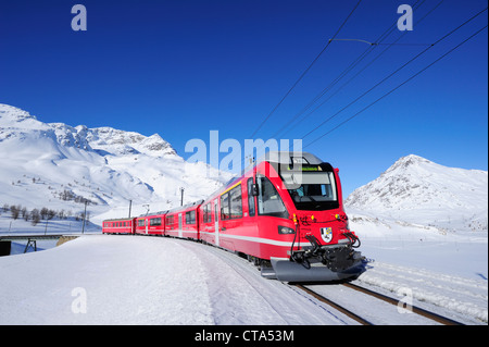 Train of Rhaetien railway driving over bridge through winter landscape ...