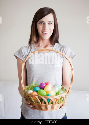 Young happy woman in Easter bunny ears holding plush carrots and basket ...