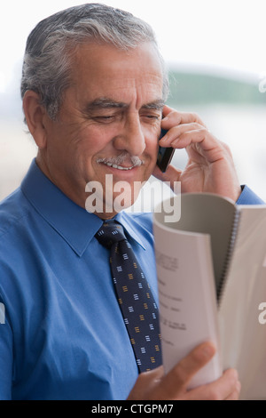Businessman reading a book while talking on his mobile phone Stock ...