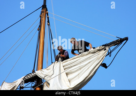 Two sailors fixing the sails high on the mast on a wooden schooner ...