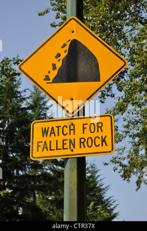 WATCH FOR FALLEN ROCK warning sign with road and rocky cliff in ...