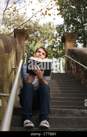 Thoughtful young man reading book on yellow background Stock Photo - Alamy