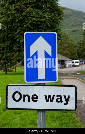 A one way road sign points towards the left on a dark night in a ...