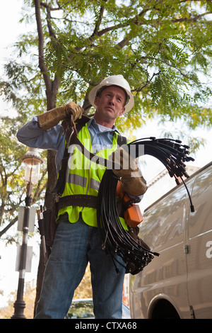 Electrician with a tool belt carrying cables on his shoulder isolated ...