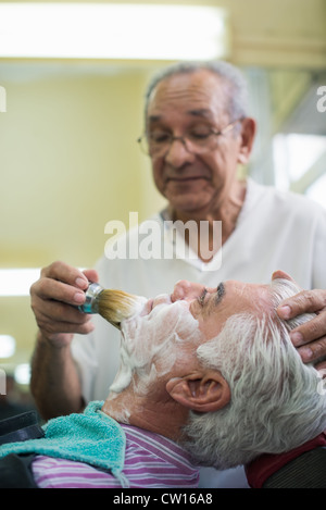 Elderly barber with shave brush applying cream to client in old style ...