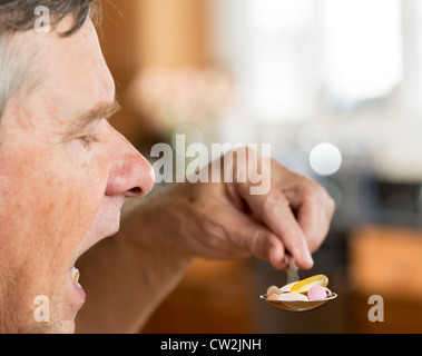 Senior caucasian male eating a spoonful of vitamin tablets for ...