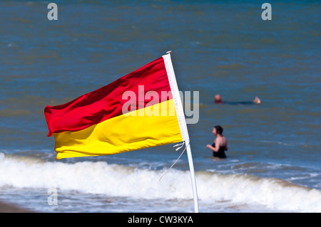Red and yellow lifeguard flag with swimmers Stock Photo - Alamy