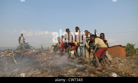 kids posing on a waste dump at the slums behind burning garbage ...