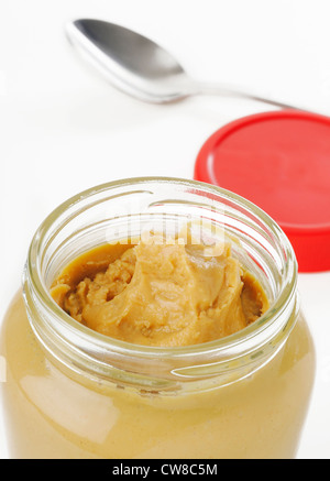 Jar of peanut butter on a white wooden table with nuts scattered nearby ...