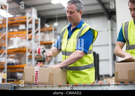 Men packing cardboard box in warehouse Stock Photo - Alamy