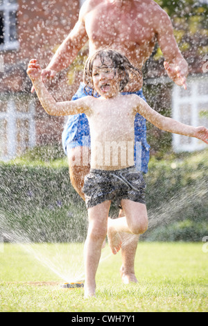 Family Running Through Garden Sprinkler Stock Photo - Alamy