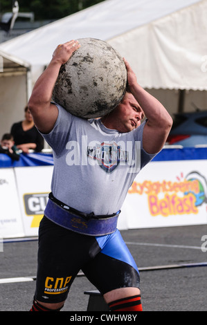 Man competing in a strongman contest lifts a very heavy Atlas Stone ...