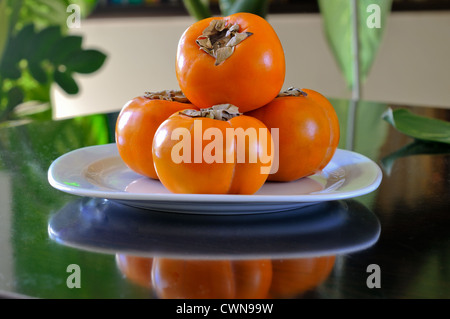 Ripe persimmon on white plate and long shadow on white table Stock ...