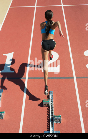 Rear view of athletic female sprinter massaging her own back muscles at ...