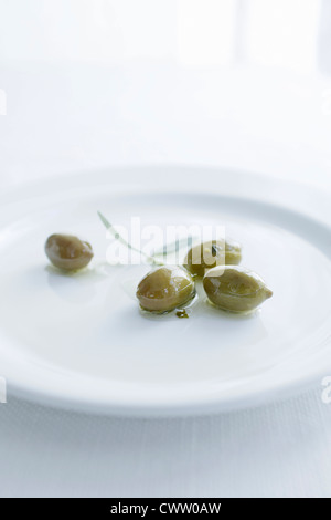 A closeup shot of green olives and an olive tree branch on a wooden ...