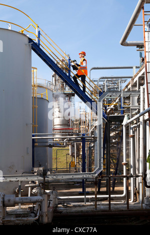 Female chemical plant process operator walkway to storage tank pipes ...